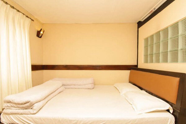 Uma cama de solteiro com cabeceira de madeira, um cobreleito branco e uma toalha dobrada ao lado esquerdo.