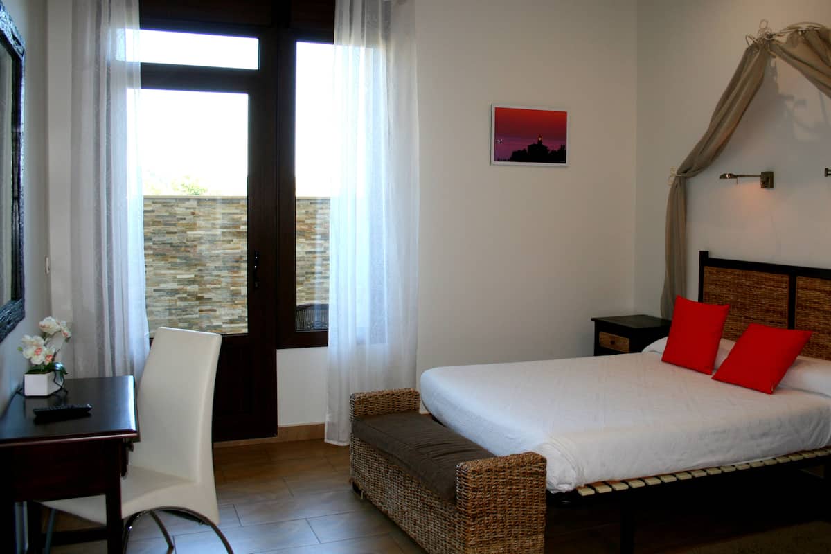 Quarto com cama, cadeira, escrivaninha e vista pela janela.
