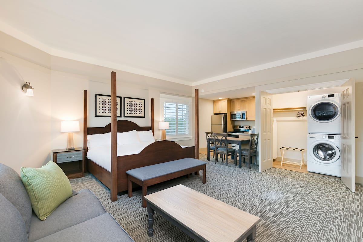 Quarto de hotel com cama de dossel, sofá, banco de madeira, escrivaninha, máquina de lavar e micro-ondas.