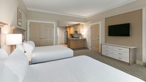 Quarto de hotel com duas camas, uma cozinha compacta, televisão e escrivaninha.