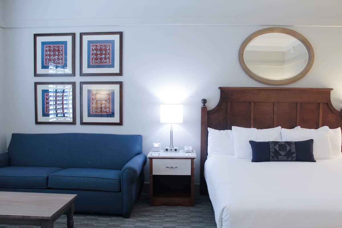 Quarto de hotel com uma cama, uma mesinha de cabeceira com abajur, um sofá azul e quadros nas paredes.
