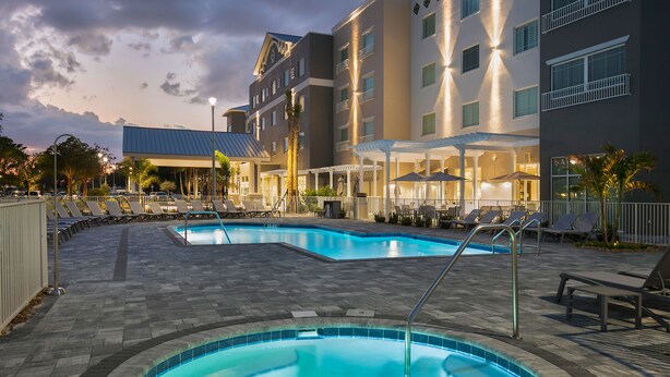 Área de piscina de hotel com espreguiçadeiras e um espaço coberto para sentar.
