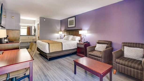Quarto de hotel com uma cama, duas mesas de cabeceira com luminárias, uma escrivaninha com cadeira e dois poltronas.