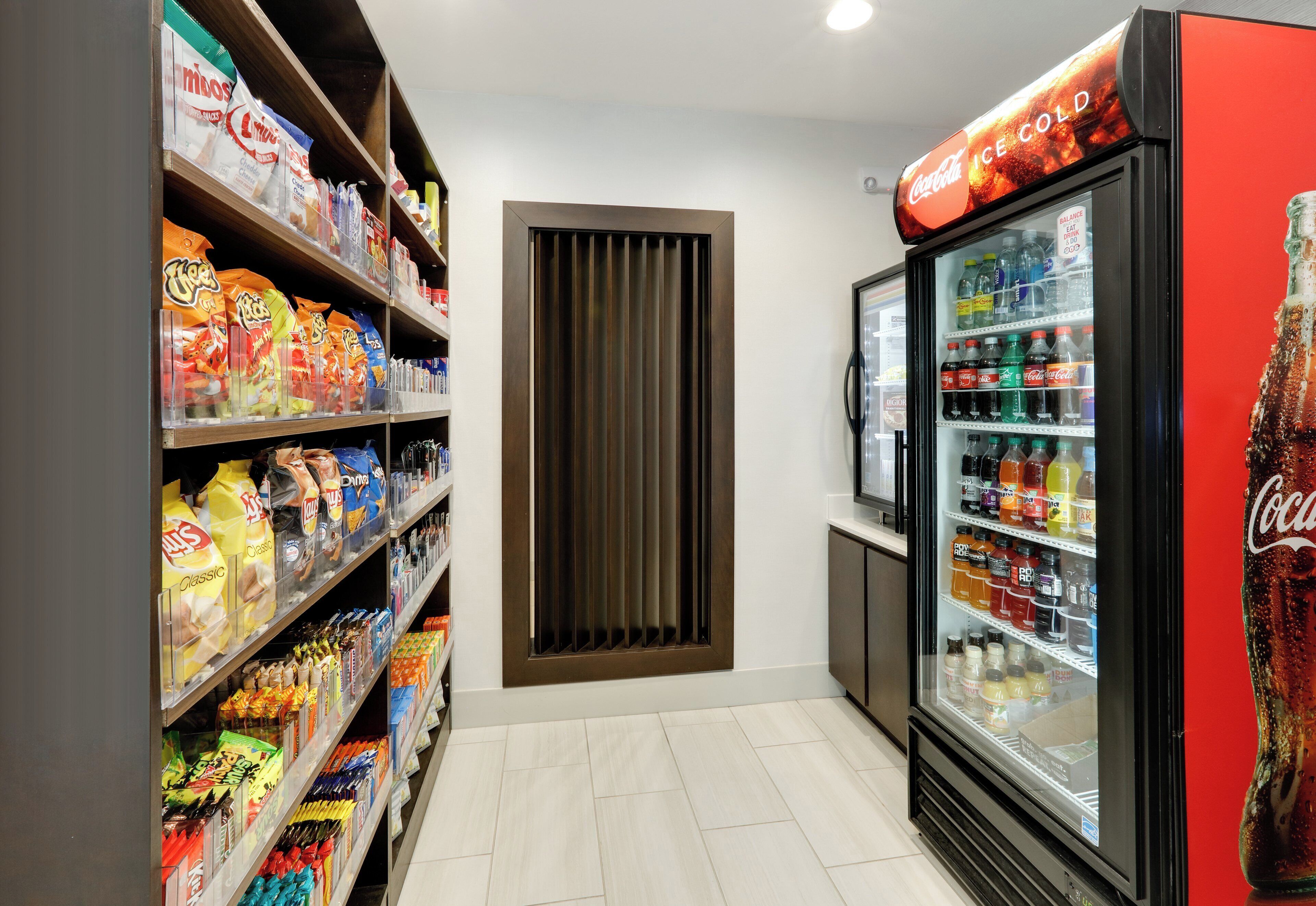Passadeira com salgadinhos e lanches diversos, geladeira repleta de refrigerantes e uma máquina de venda automática de Coca-Cola.