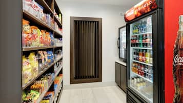 Passadeira com salgadinhos e lanches diversos, geladeira repleta de refrigerantes e uma máquina de venda automática de Coca-Cola.