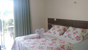 Uma cama bem arrumada com roupa de cama florida, cabeceira e vista para o exterior atrav és de uma janela.