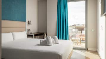 Quarto de hotel com uma cama grande, uma escrivaninha, uma cadeira e vista para a cidade por uma janela ampla.