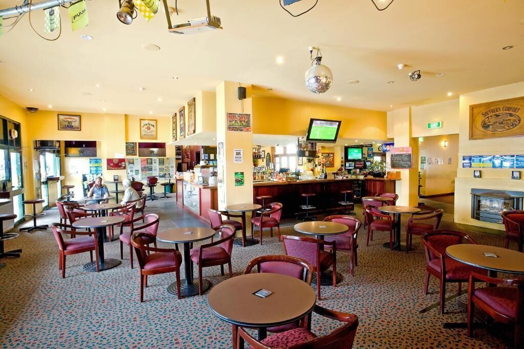 Uma área de bar com várias mesas e cadeiras, uma tela de televisão e uma lareira.