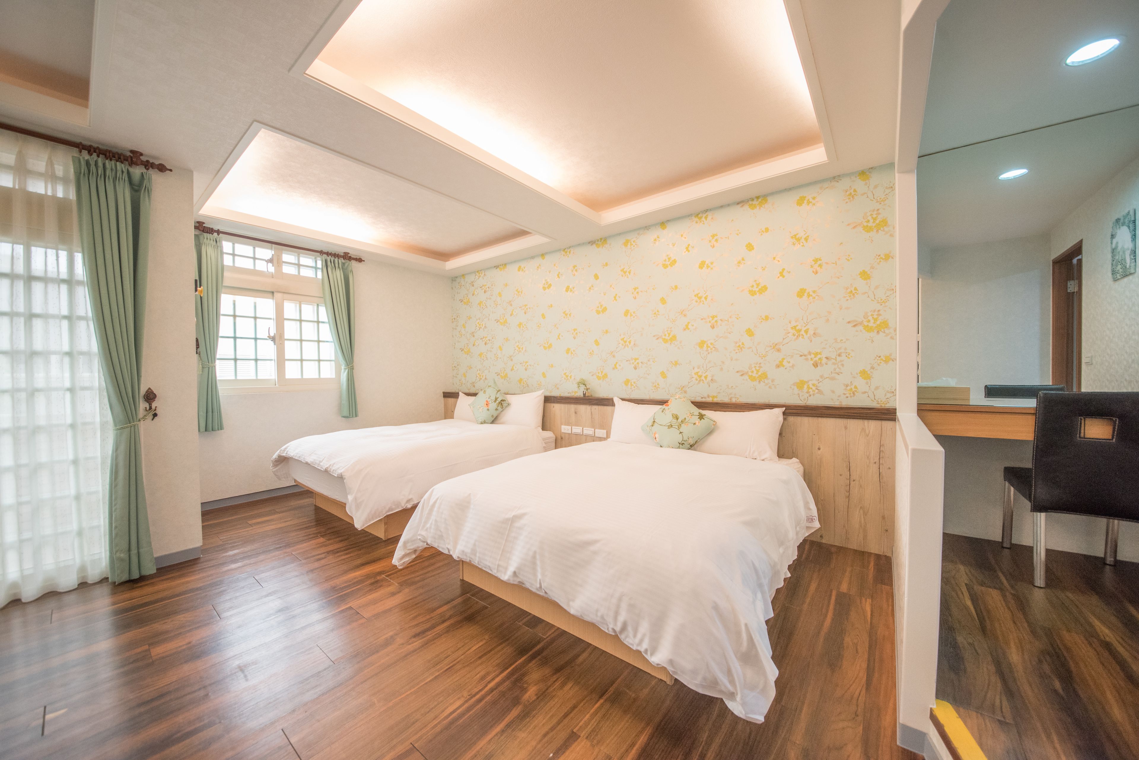 Quarto de hotel com duas camas, piso de madeira, uma escrivaninha e uma cadeira.