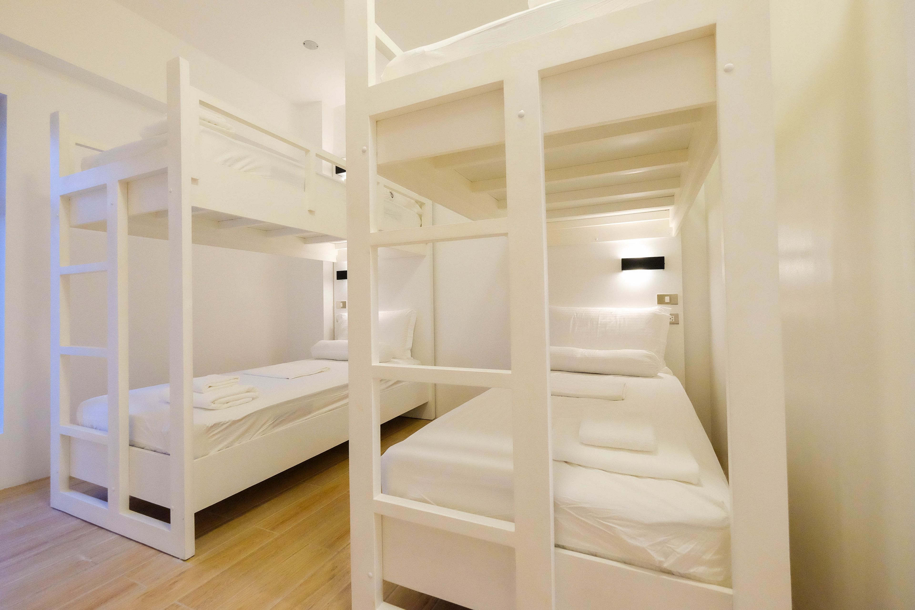 Quarto com beliches, piso de madeira e decoração em tons de branco.