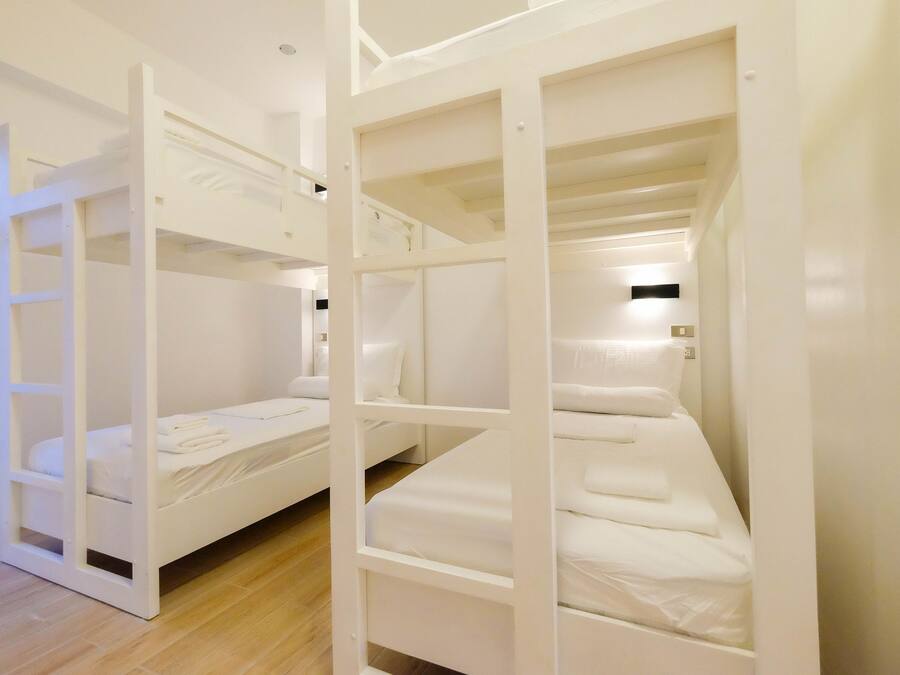 Quarto com beliches, piso de madeira e decoração em tons de branco.