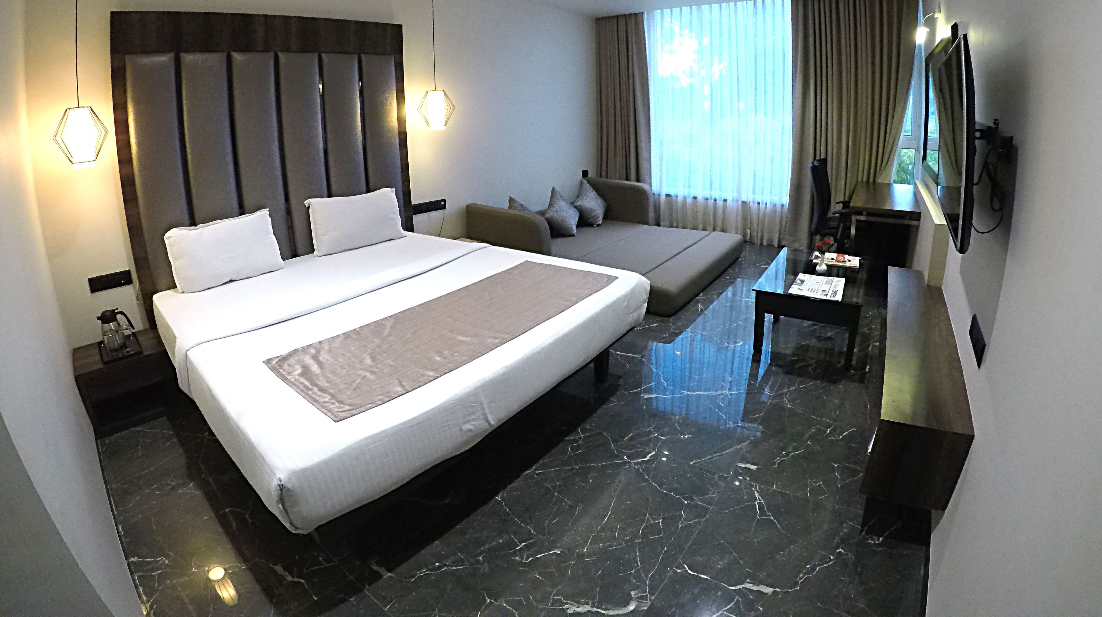 Quarto de hotel com uma cama grande, um sofá, uma mesinha, uma televisão e uma janela com cortinas.
