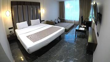 Quarto de hotel com uma cama grande, um sofá, uma mesinha, uma televisão e uma janela com cortinas.