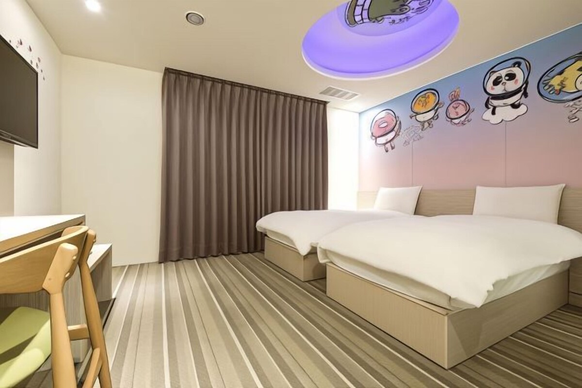 Quarto de hotel com cama, escrivaninha e televisão.
