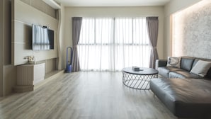 Uma sala de estar moderna com televisão de tela plana, uma mesa de centro redonda, um sofá e uma janela grande com cortinas.