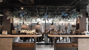 Uma área de bar com duas mesas para acomodar clientes, teto decorativo e um letreiro com a palavra 'WHOPS'.