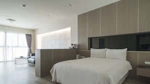 Quarto de hotel moderno com uma cama grande, uma mesa de trabalho e uma janela ampla com cortinas.