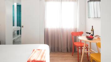 Quarto de hotel com cama, mesa com cadeiras, uma garrafa de vinho e uma cesta de frutas.