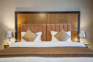 Cama bem arrumada com cabeceira de madeira, duas luminárias de apoio e um edredom marrom.