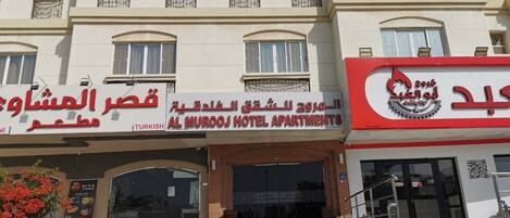 Exterior do Al Murooj Hotel Apartments, com um letreiro em turco e árabe, uma escadaria que leva à entrada e um código QR no lado direito.