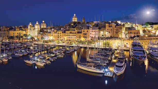 Uma marina com barcos atracados, paisagem urbana com edifícios históricos e uma torre do relógio imponente.