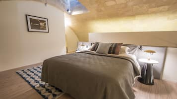 Quarto com cama, mesa de cabeceira, abajur, tapete estampado e um quadro na parede.