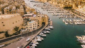 Uma marina com vários barcos atracados, rodeada por edifícios históricos e uma fortificação imponente.
