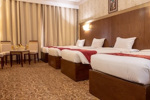 Quarto de hotel com três camas, uma mesa de jantar com cadeiras e uma mesinha com uma fruteira e bebidas.