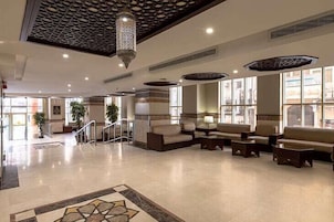 Um hall amplo com teto alto, design de padrão no teto e grandes janelas que permitem a entrada de luz natural.