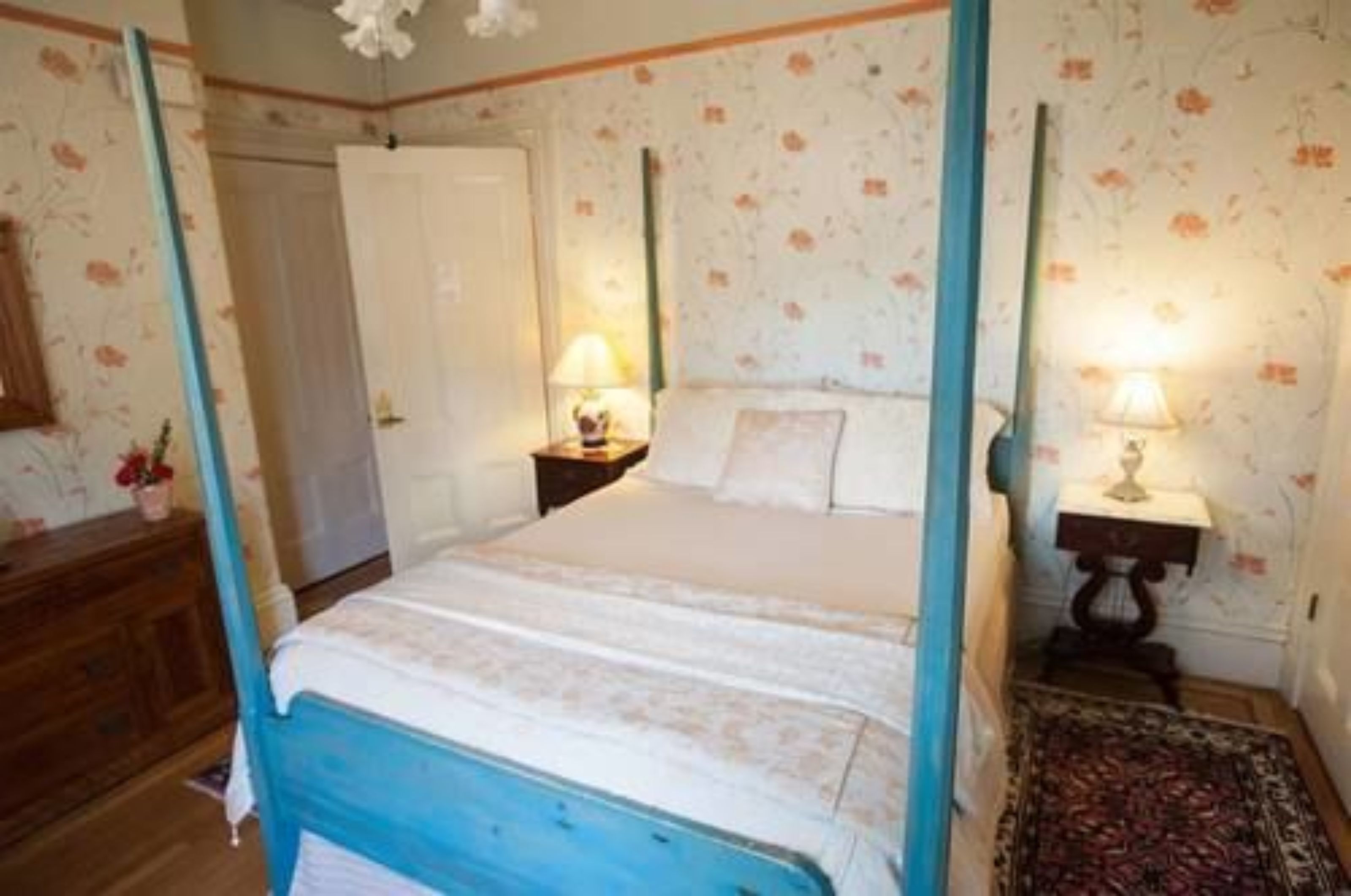 Quarto com cama de dossel, papel de parede floral e duas luminárias de cabeceira.