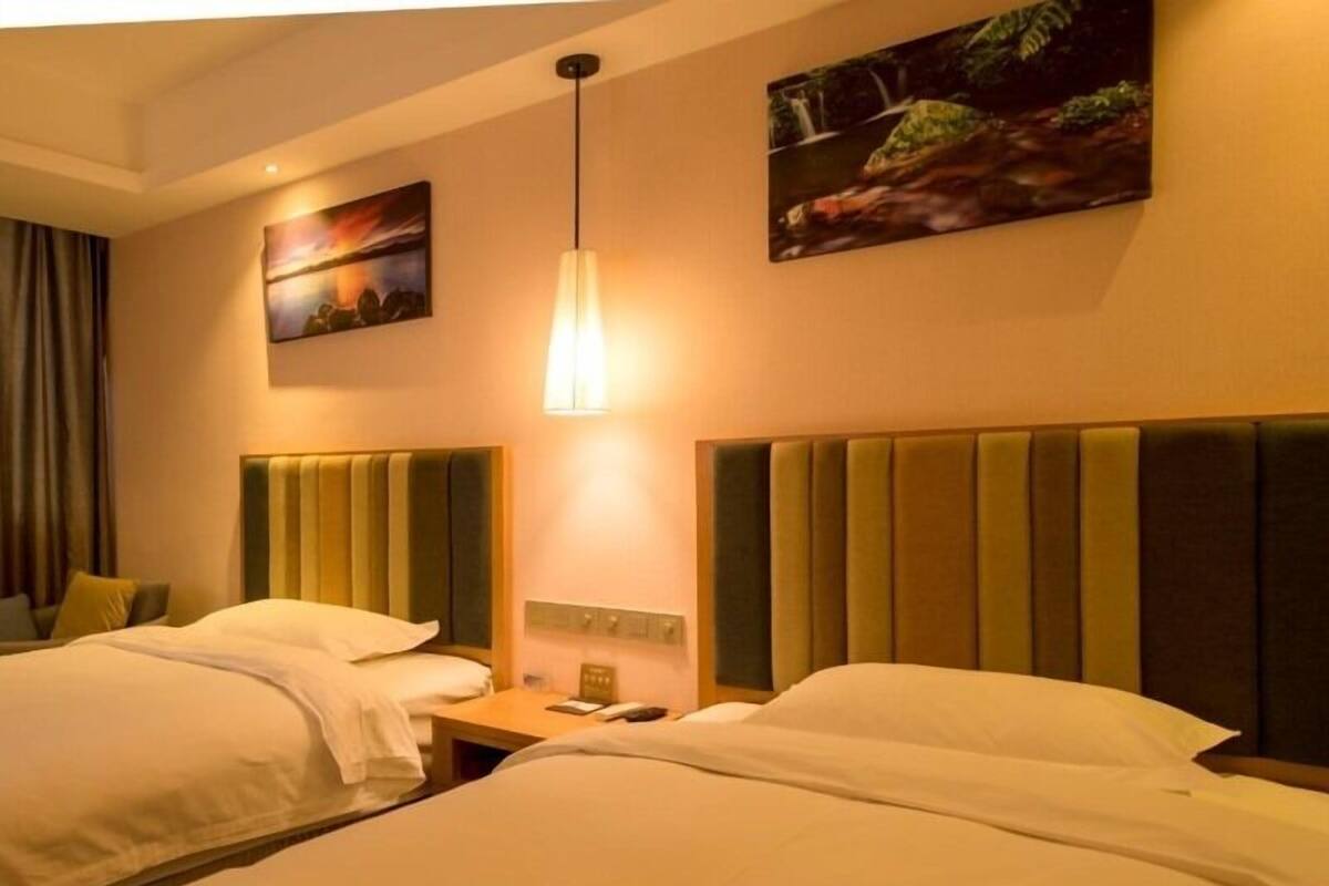 Quarto de hotel com duas camas, uma mesa de cabeceira, um abajur e duas pinturas na parede.