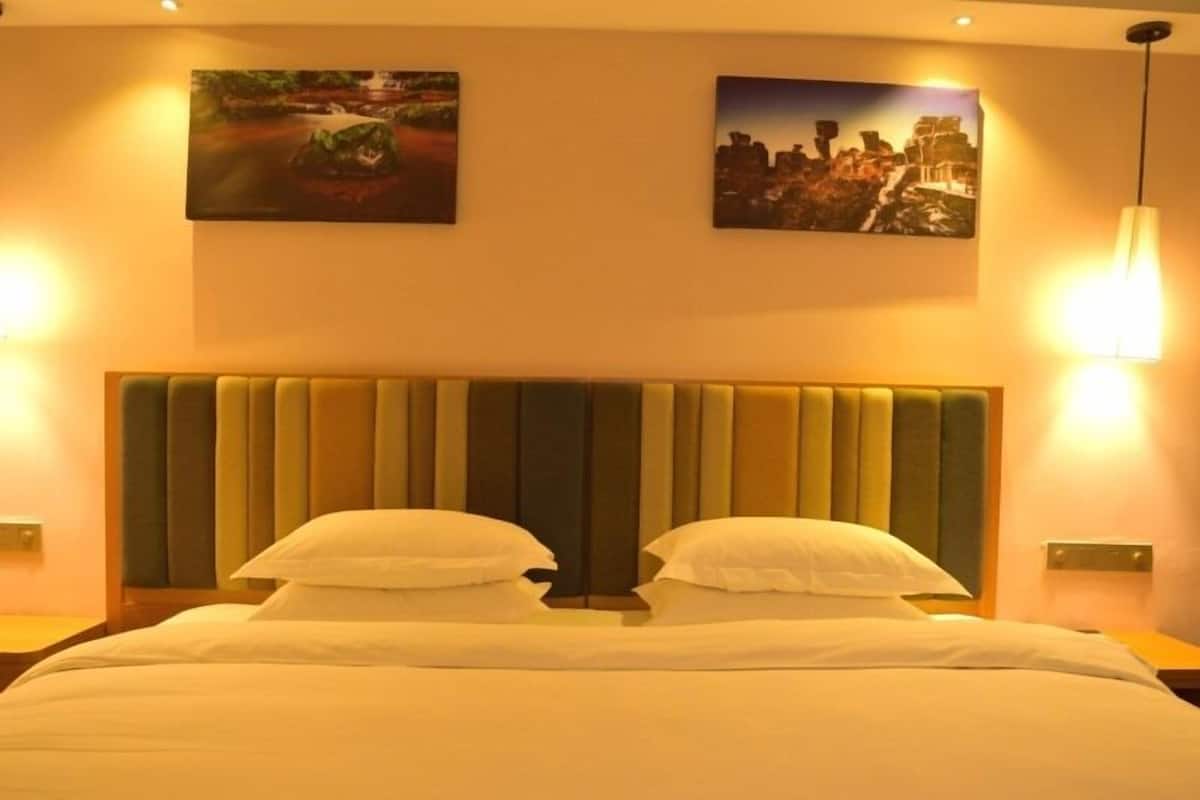 Quarto de hotel com uma cama grande, duas luminárias fixadas na parede e duas molduras com quadros acima da cama.