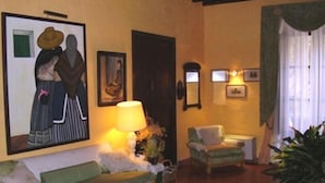 Uma sala de estar acolhedora com um sofá verde, uma mesinha com abajur, um quadro emoldurado e um vaso com planta.