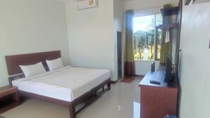 Quarto de hotel com cama, escrivaninha com computador, cadeira e janela com cortinas.