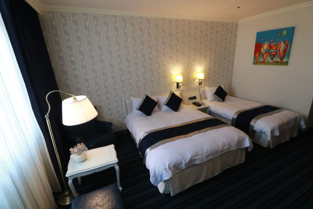Quarto de hotel com duas camas, uma escrivaninha, um abajur e um quadro na parede.