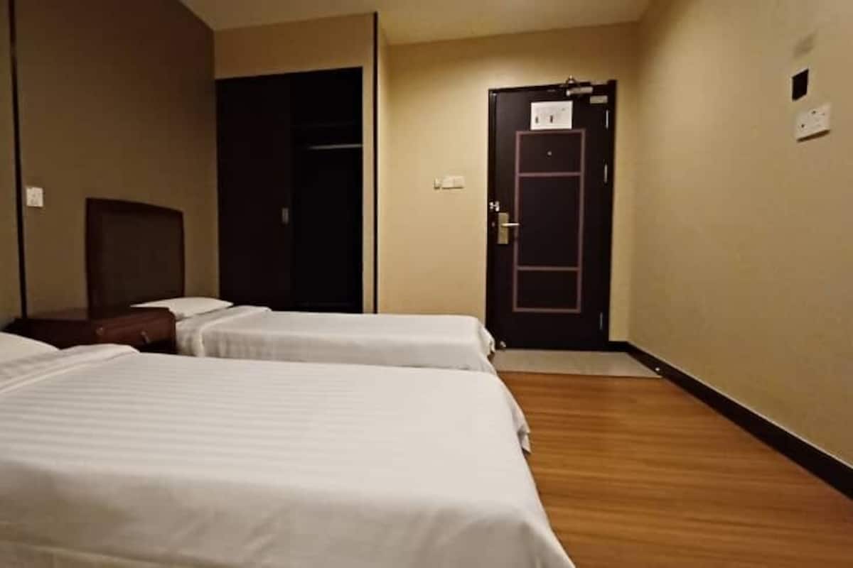 Quarto de hotel com duas camas, piso de madeira, uma porta e um armário.