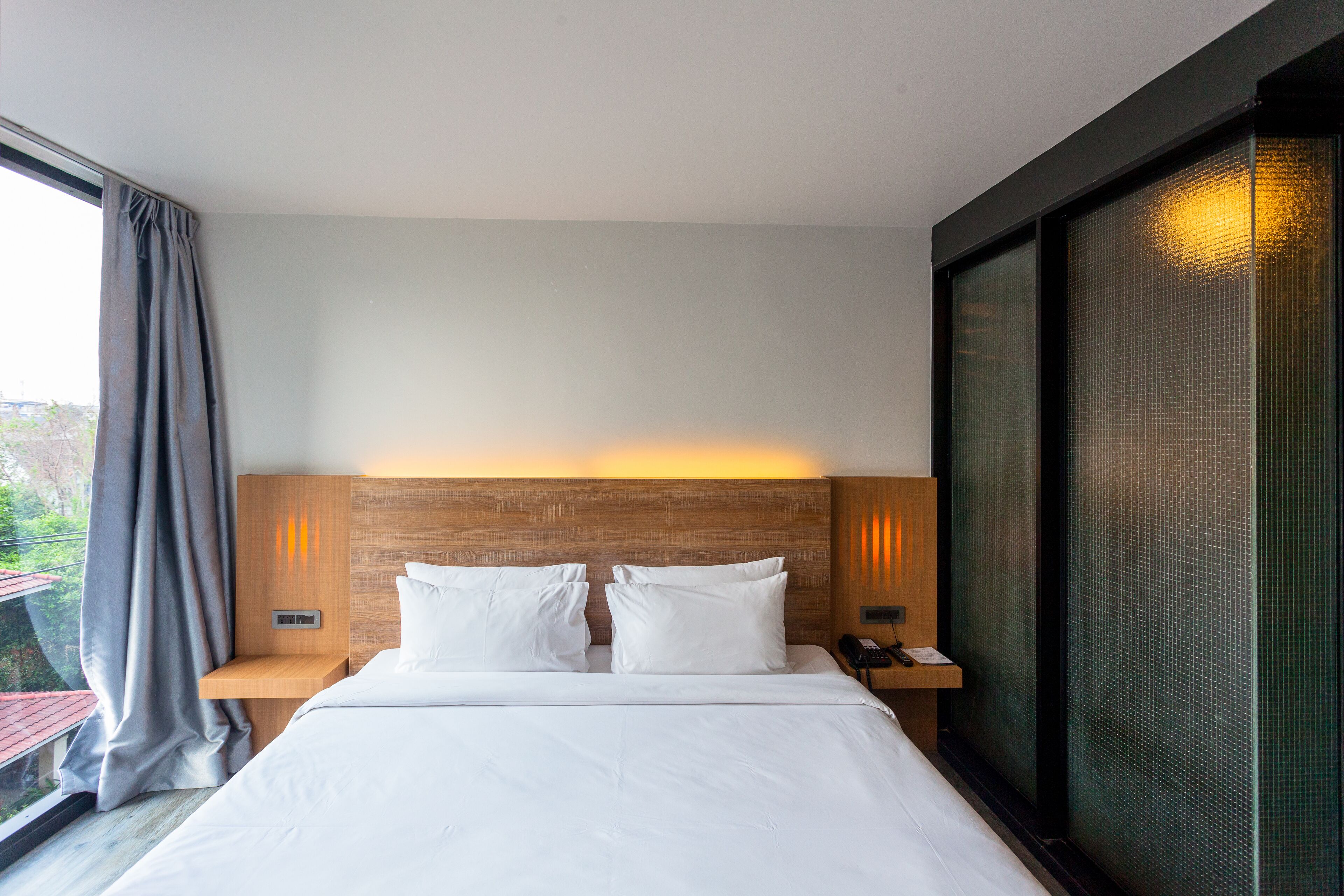 Quarto de hotel moderno com uma cama grande, cabeceira de madeira e vista através de uma janela ampla.