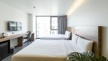 Quarto de hotel com uma cama, uma escrivaninha com cadeira, televisão e uma janela grande com cortinas.