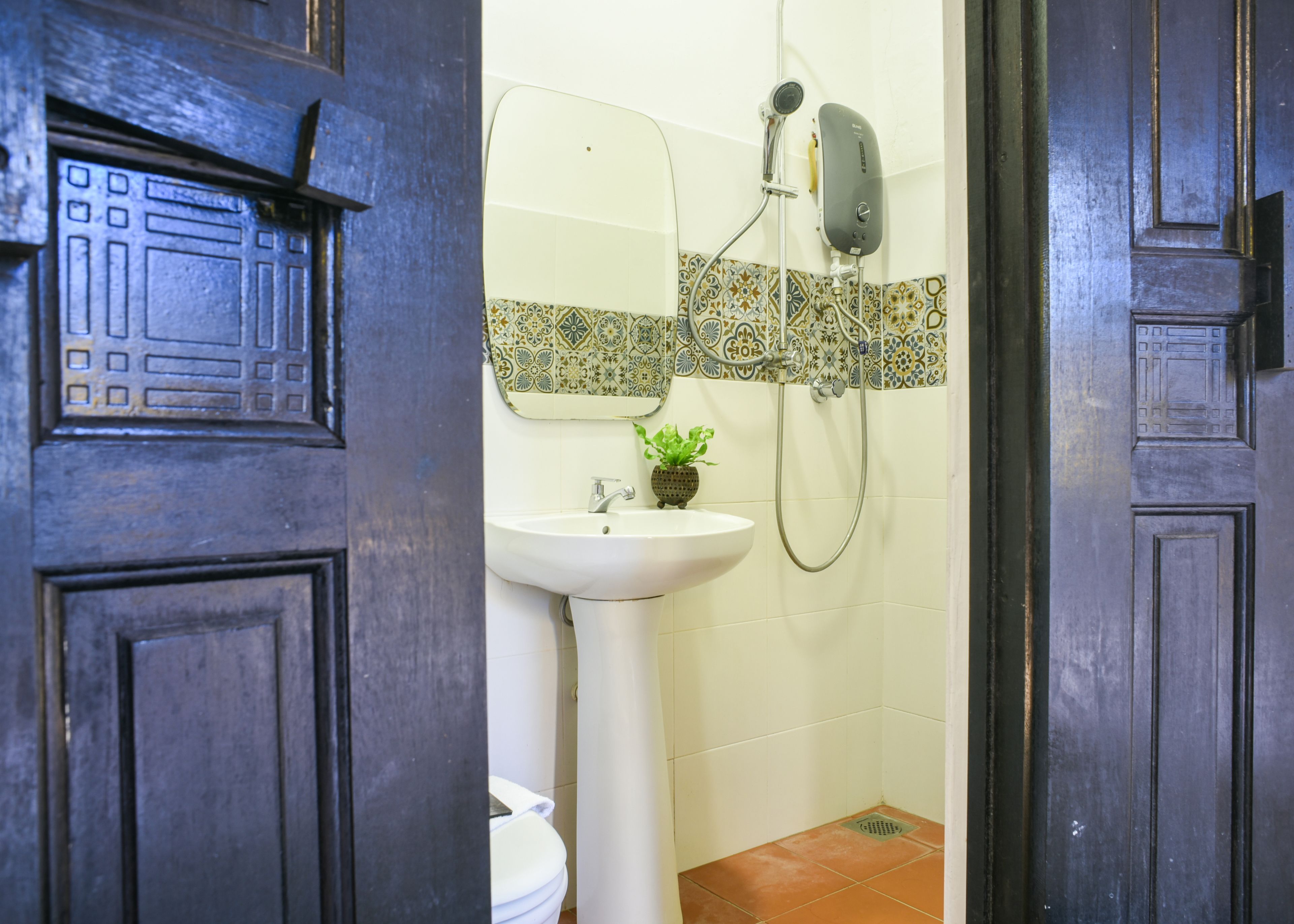 Casa de banho com lavatório branco, chuveiro manual, sanita e painel de azulejos decorativos.