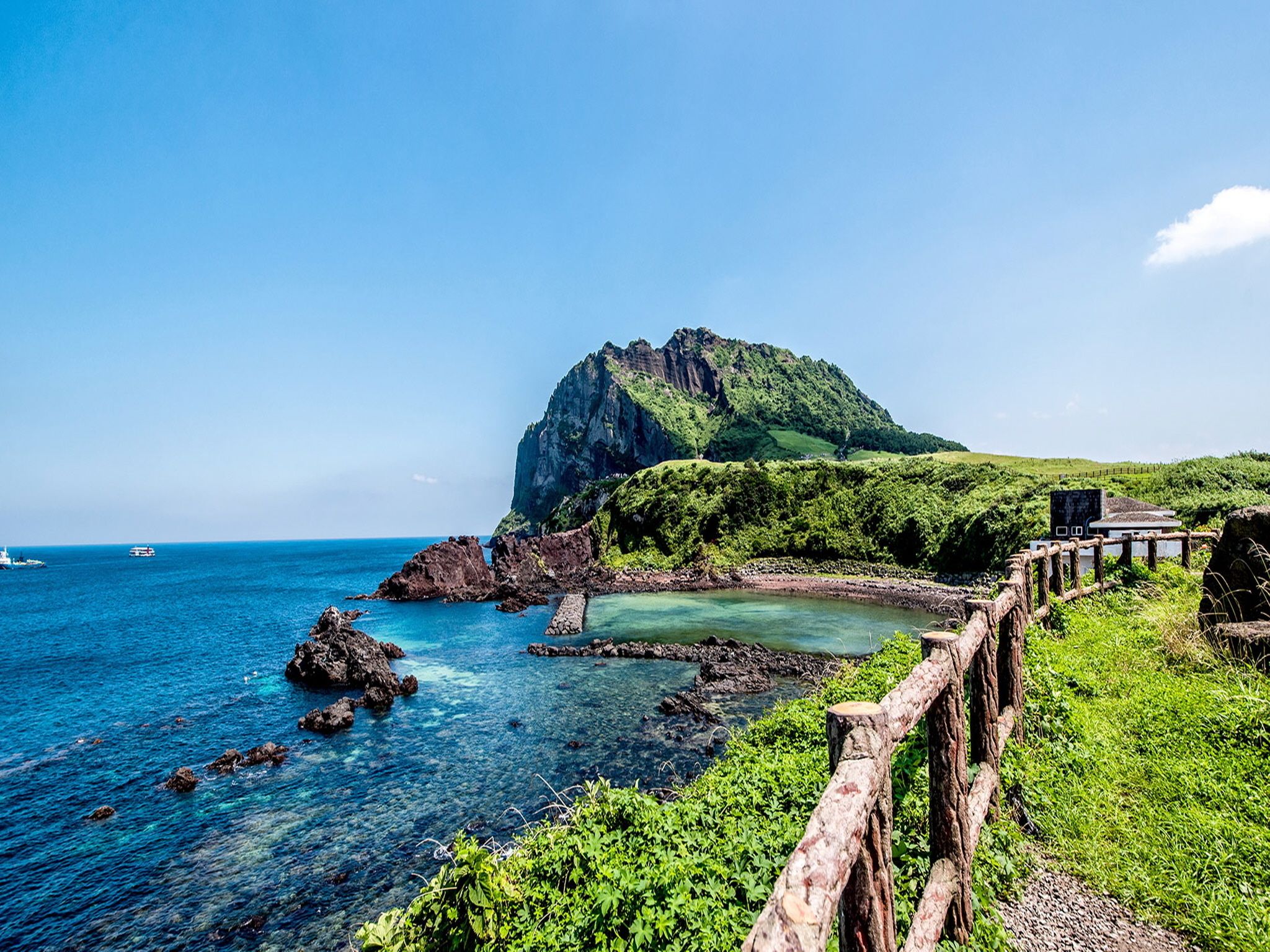 Paisagem costeira com um imponente penhasco rochoso, águas azuis cristalinas e uma cerca de madeira.