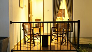 Uma varanda com guarda-corpo preto, duas cadeiras de madeira e uma pequena mesa.