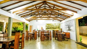 Uma sala de jantar ampla, com mesas e cadeiras de madeira, teto alto com vigas aparentes e um mural na parede.