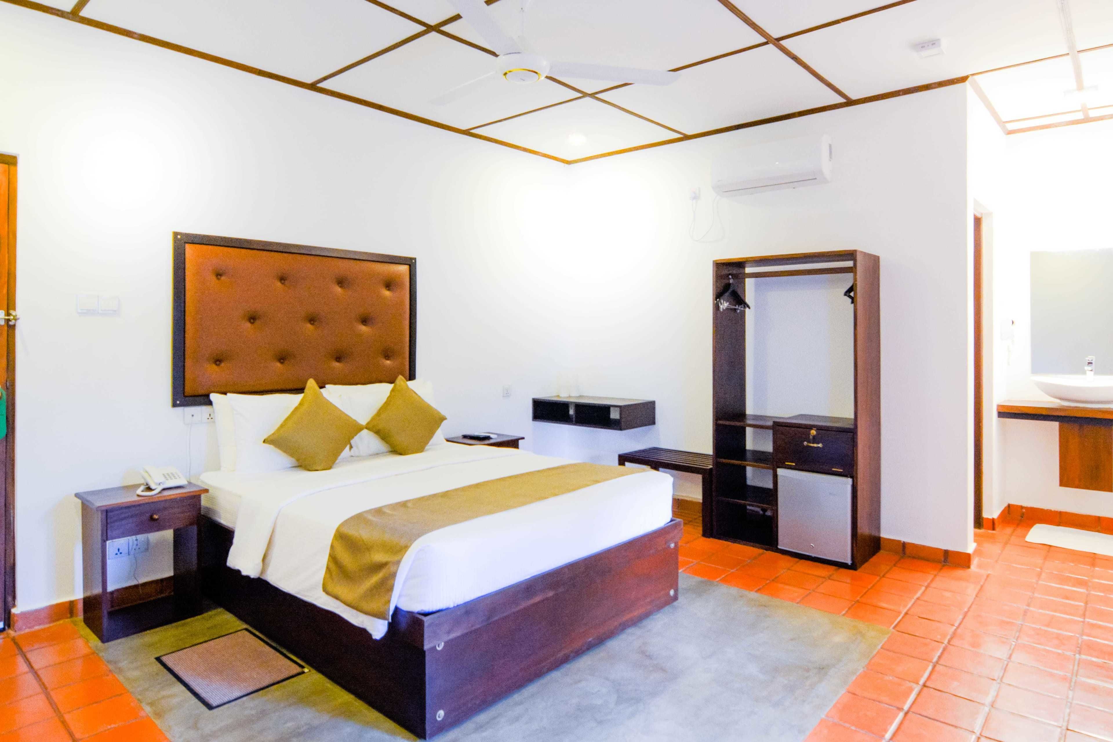 Quarto de hotel com uma cama grande, mesa de cabeceira com telefone, armário e banheiro com pia e espelho.