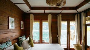 Quarto com uma cama grande, paredes de madeira, vista para a água e uma rede.