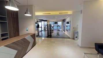 Academia moderna com equipamentos de ginástica, balcão de recepção e uma ampla janela com vista para a cidade.