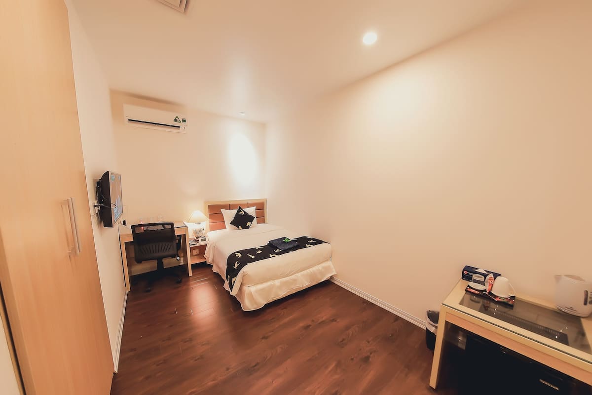 Quarto com cama, mesa de cabeceira, escrivaninha, cadeira e ar condicionado.
