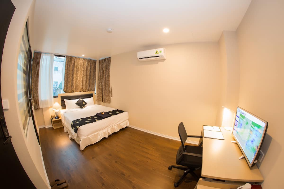 Quarto de hotel com cama, escrivaninha, cadeira e monitor de computador.