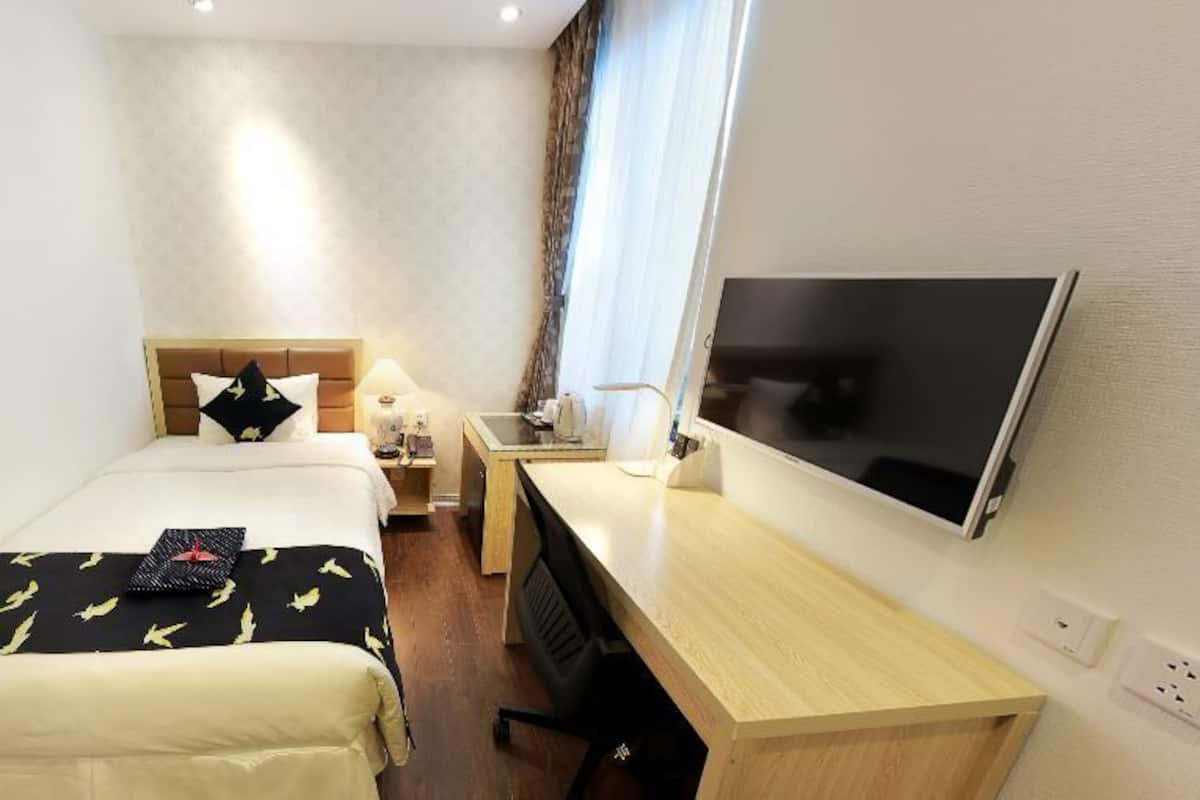 Quarto de hotel com uma cama, escrivaninha, televisão e janela com cortinas.