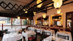 Restaurante com mesas redondas preparadas para refeições, com centros de mesa de velas e um ambiente acolhedor e convidativo.