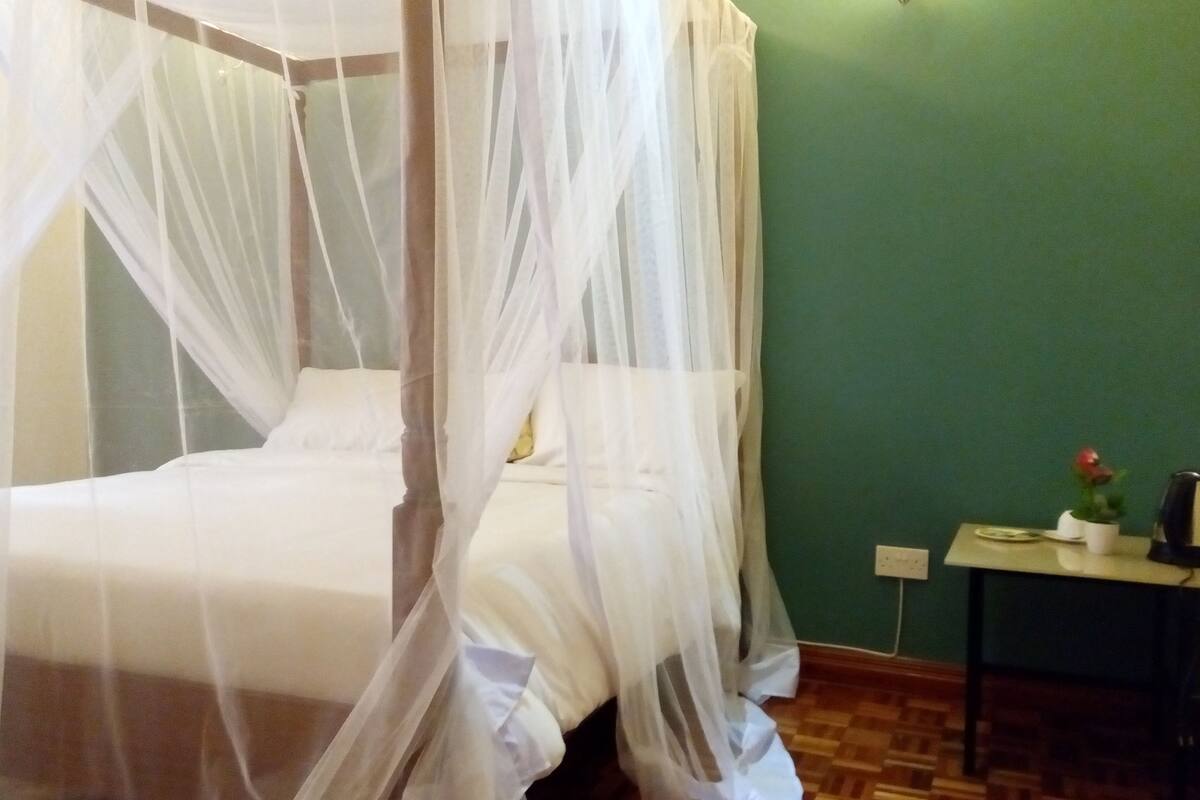 Uma cama com dossel, uma mesa de cabeceira com uma planta e uma tomada na parede.